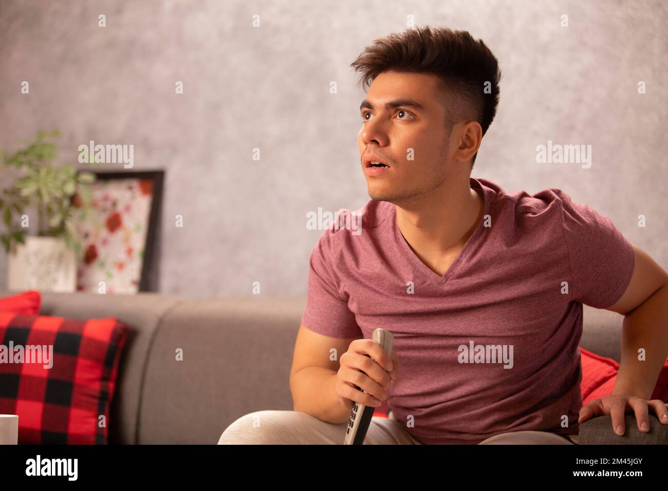Excited young man watching TV while sitting on sofa in living room ...
