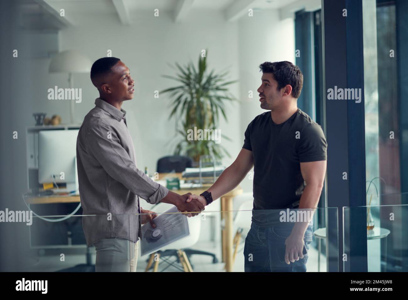 Ive heard good things. two young businessmen shaking hands in a modern ...