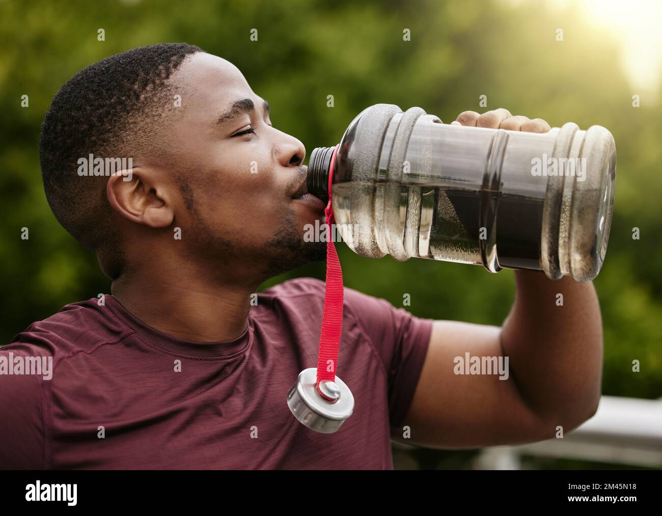 Fitness, nature and man drinking water after a workout in a park for ...