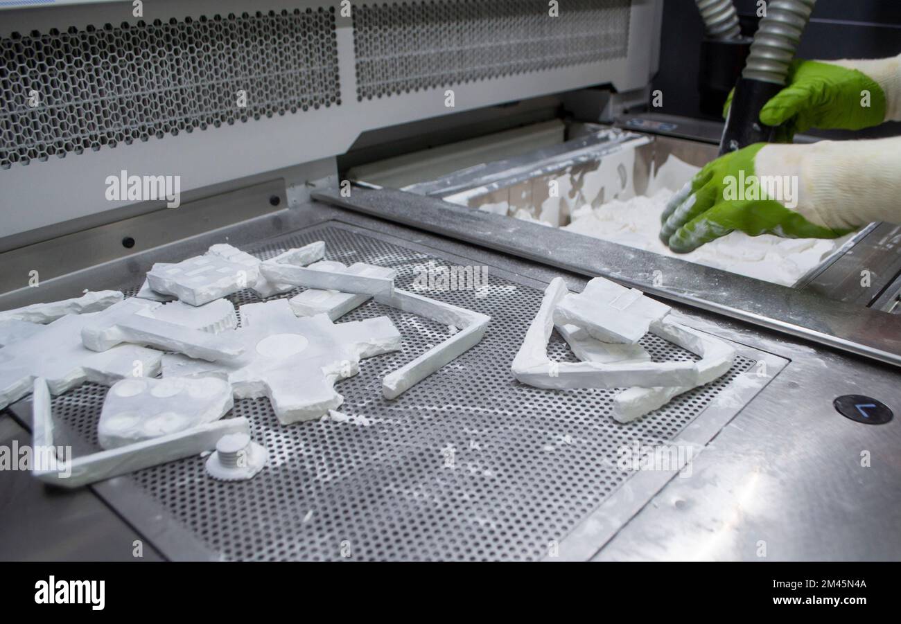 Male worker taking out models from white polyamide powder in working ...