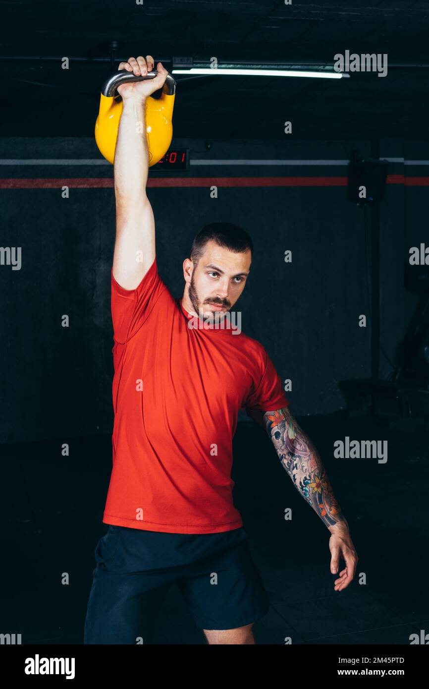 Vertical portrait of a string Man lifting weight with a kettlebell ...