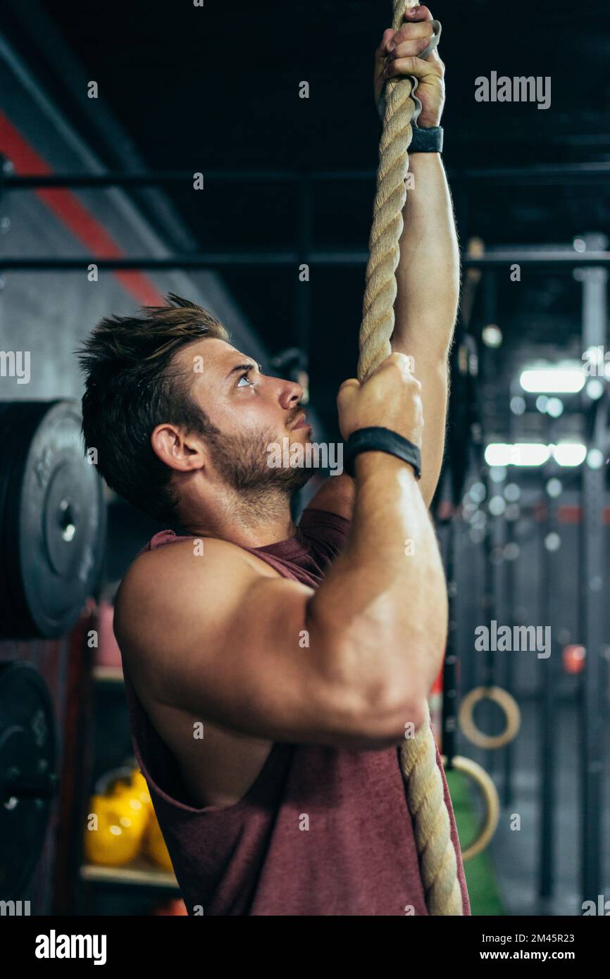 Vertical close up photo of a strong man climbing a rope in a gym Stock ...