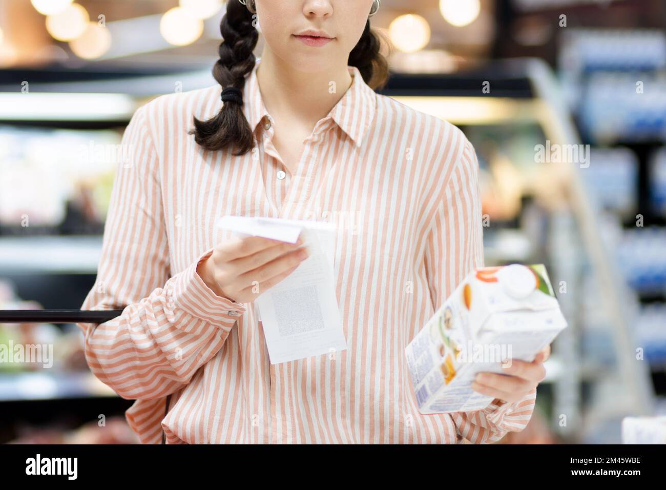 Pretty young Caucasian woman looks at shopping list and holds product ...