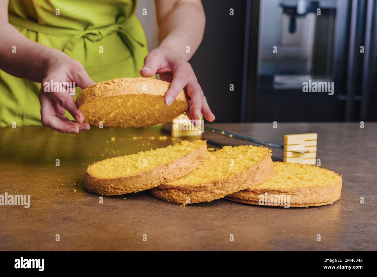 Female baker slicing traditional sponge cake into layers using special ...