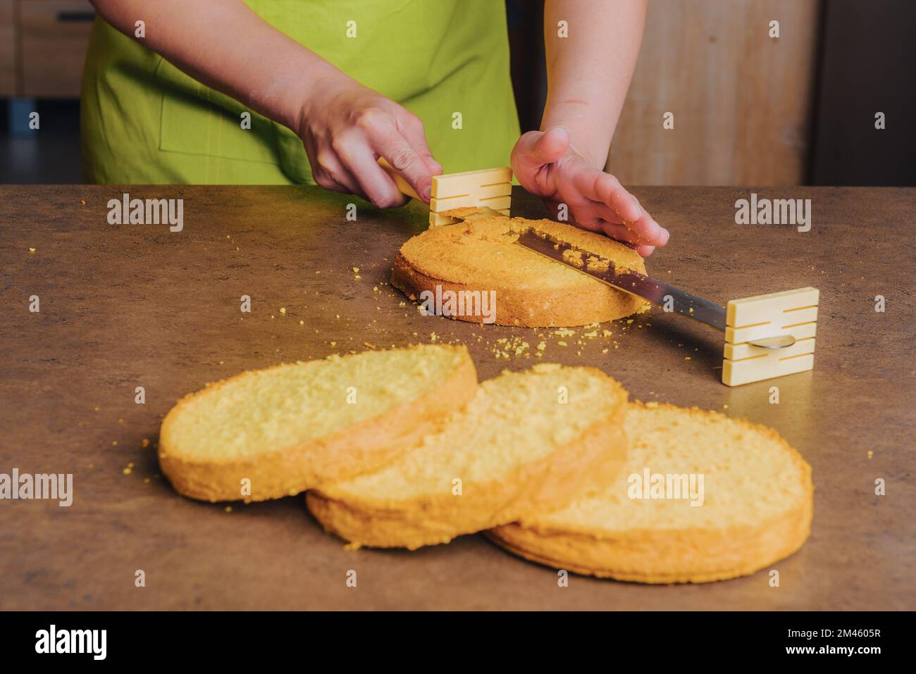 Female baker slicing traditional sponge cake into layers using special ...