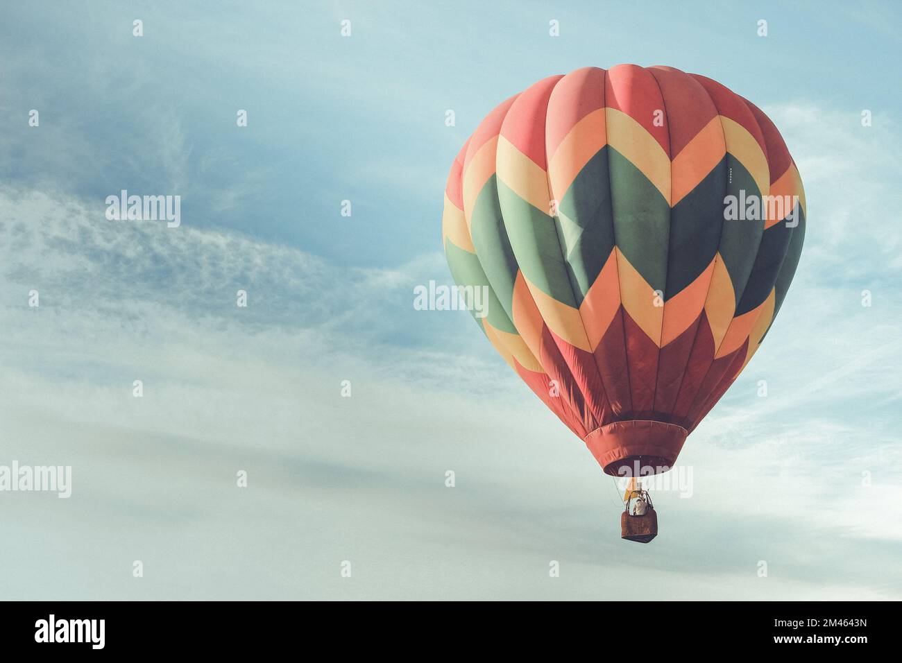 A colorful hot air balloon flying in the blue sky covered in clouds in ...