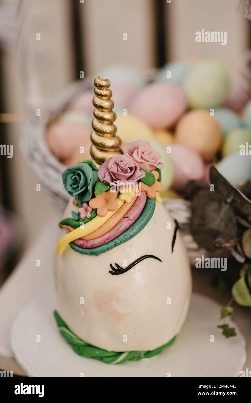 A vertical shot of a unicorn cake with colorful Easter eggs in the ...