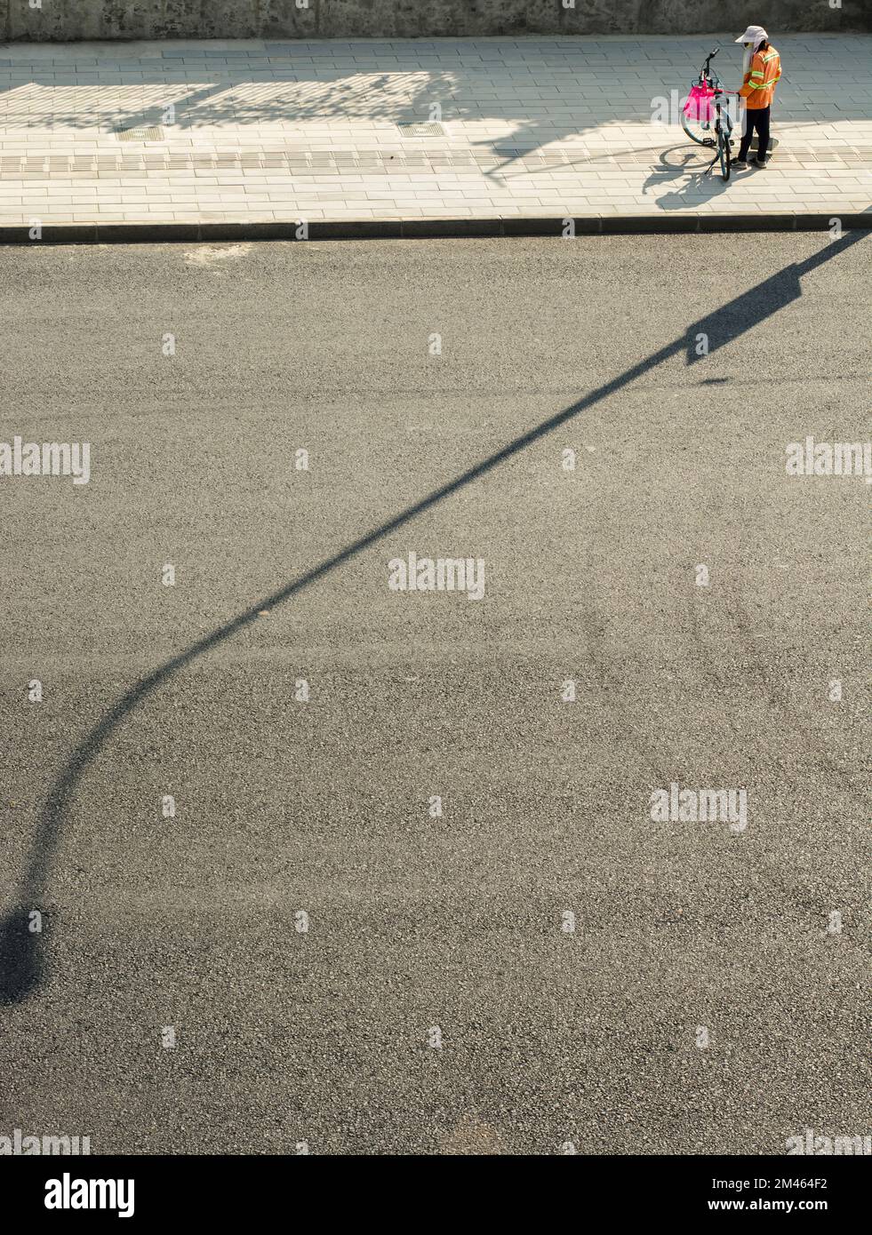 A drone shot of a girl with bicycle on a street with a shadow of street ...
