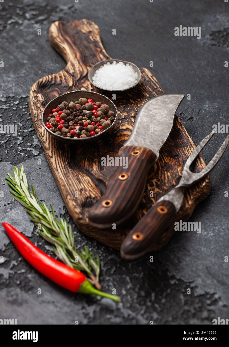 Fork and knife on chopping board with pepper and salt with rosemary on ...