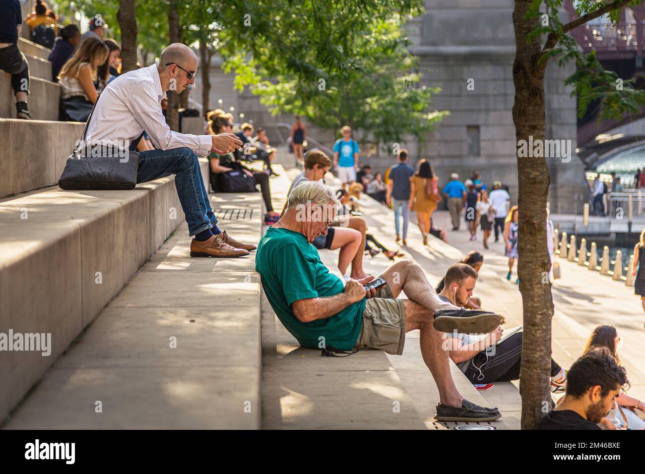 People sit on the steps of a riverside public space on the Chicago ...