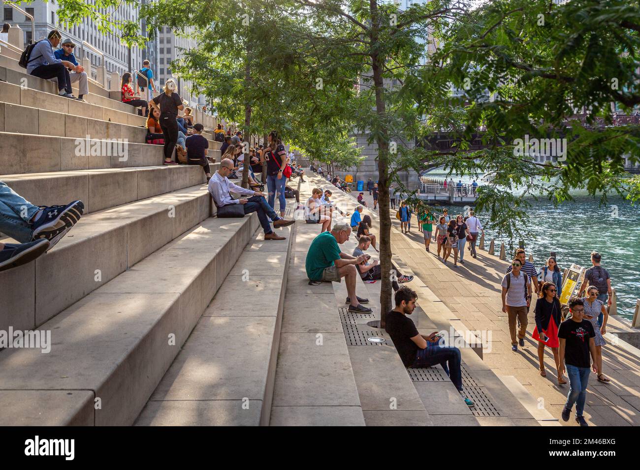 People sit on the steps of a riverside public space on the Chicago ...