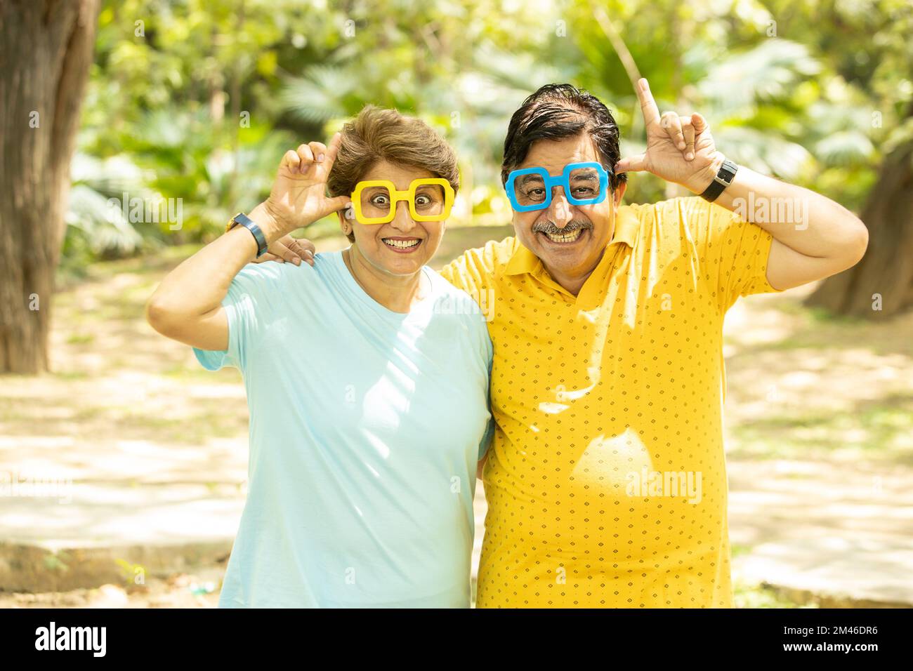 Portrait of crazy excited funny senior indian couple wearing funky eye glasses outdoor at park ...