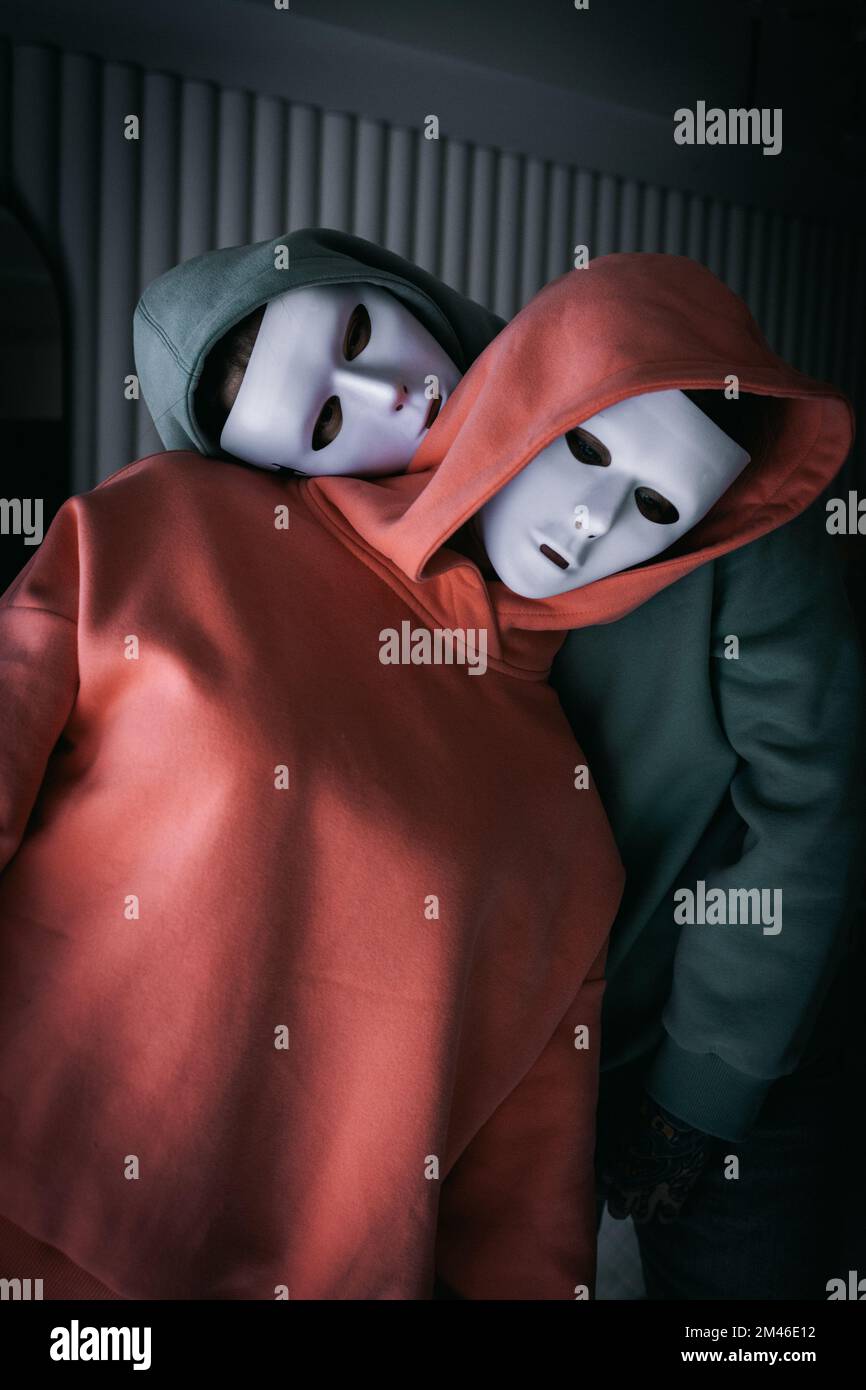Portrait of two people in white theatrical masks and hood on black ...