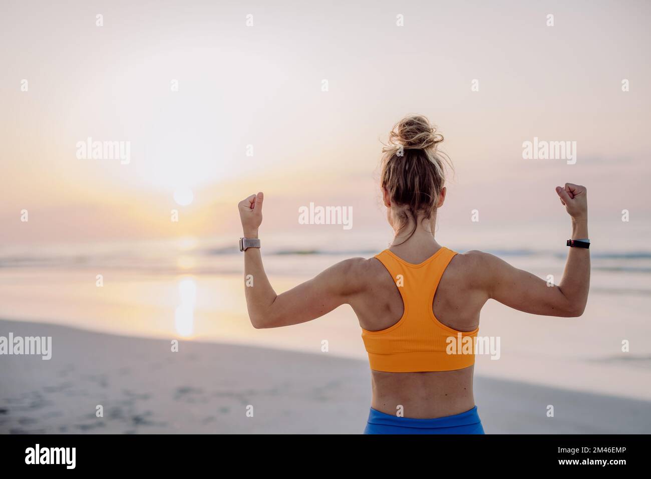 Rear view of young woman taking exercises at beach, morning routine and ...