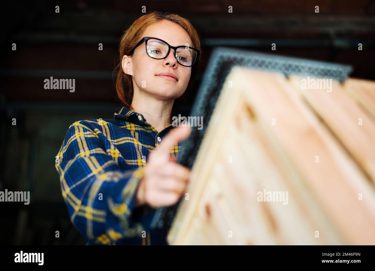 Young woman wearing glasses measuring wooden object using angle rulet ...