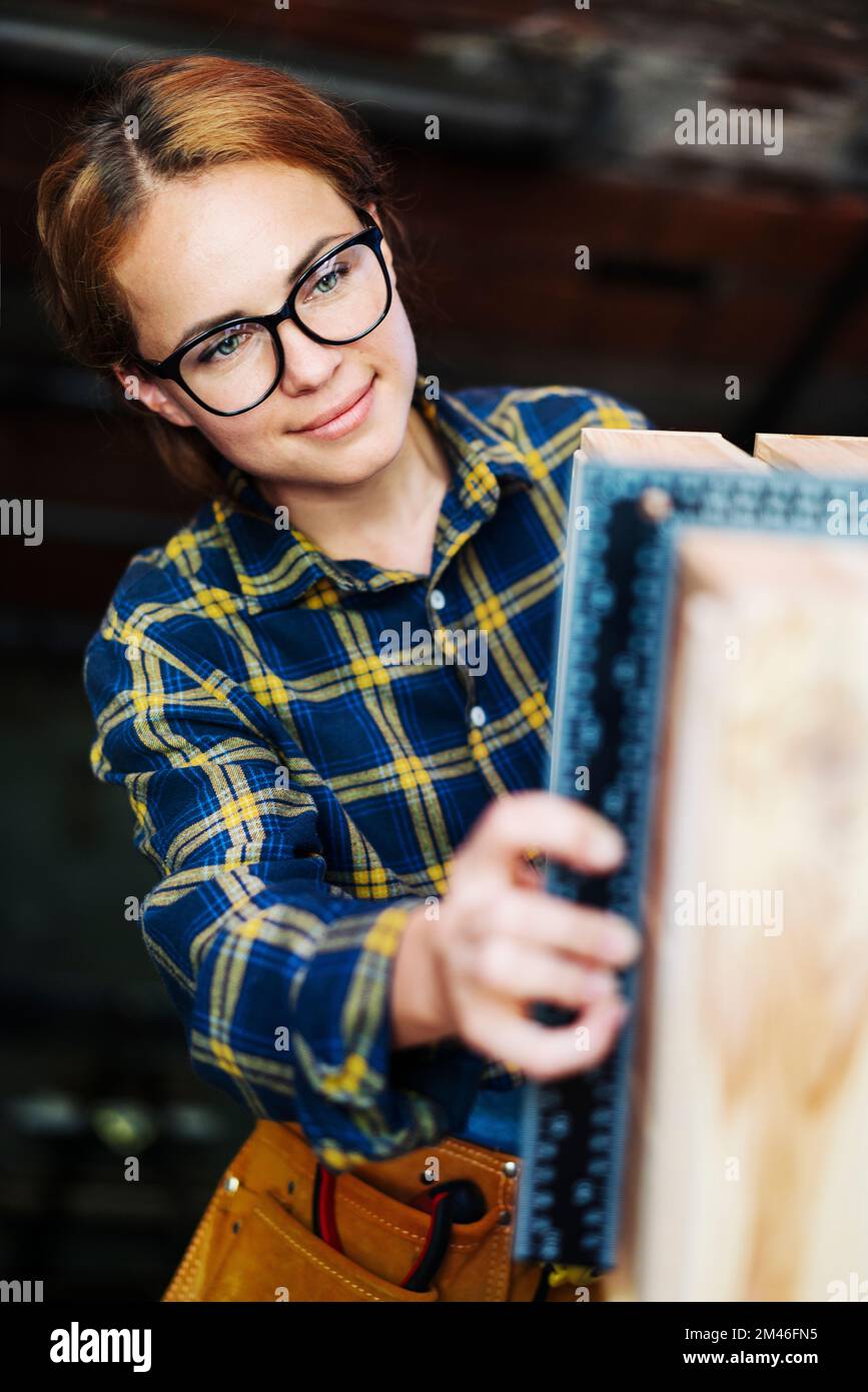 Young woman wearing glasses measuring wooden object using angle rulet ...