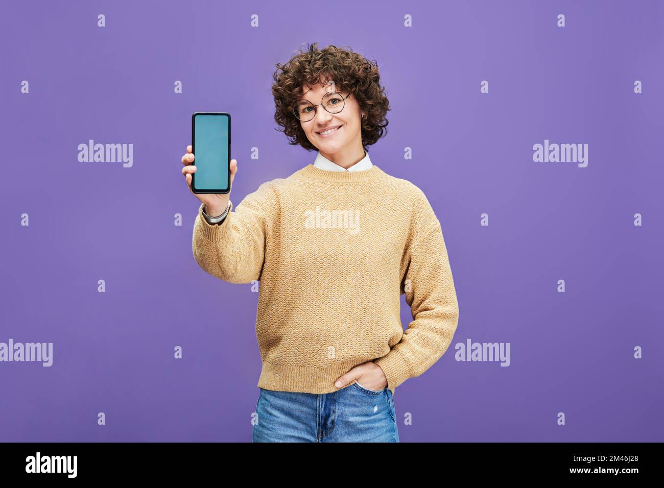 Young smiling brunette woman holding smartphone with blank blue screen ...