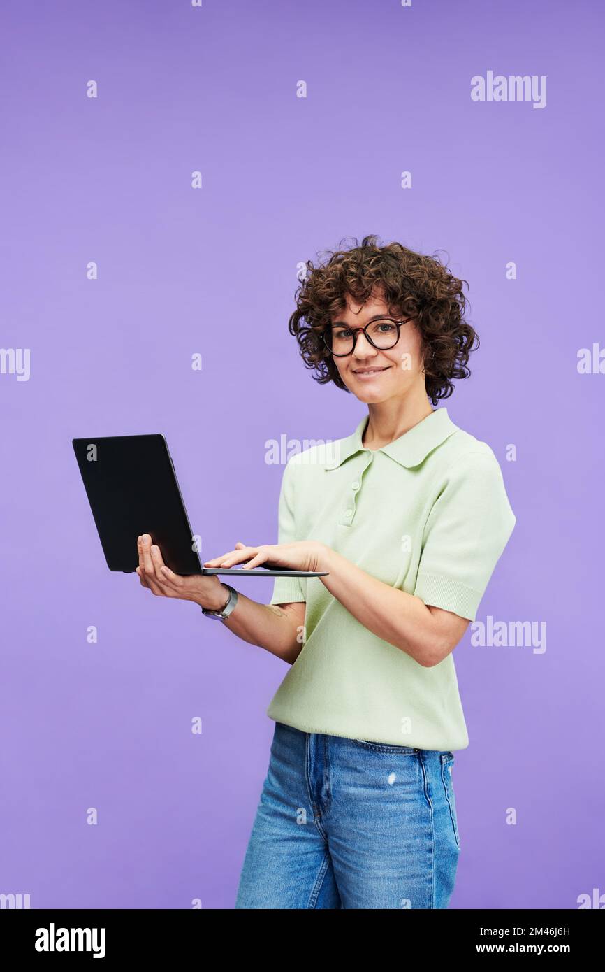Young modern woman in jeans and shirt holding laptop while standing in ...