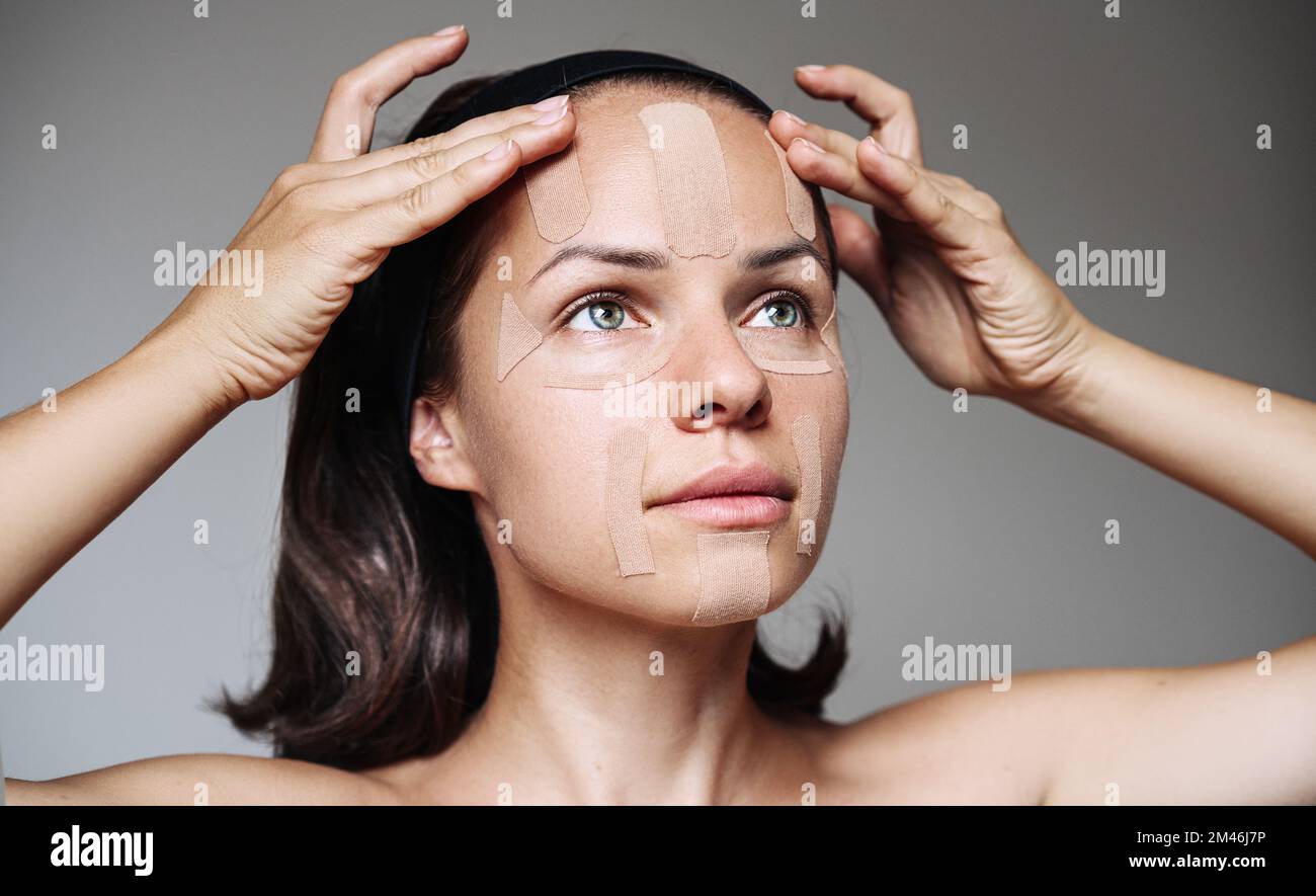 Young adult woman applying facial kinesiology tape on her face, facial ...