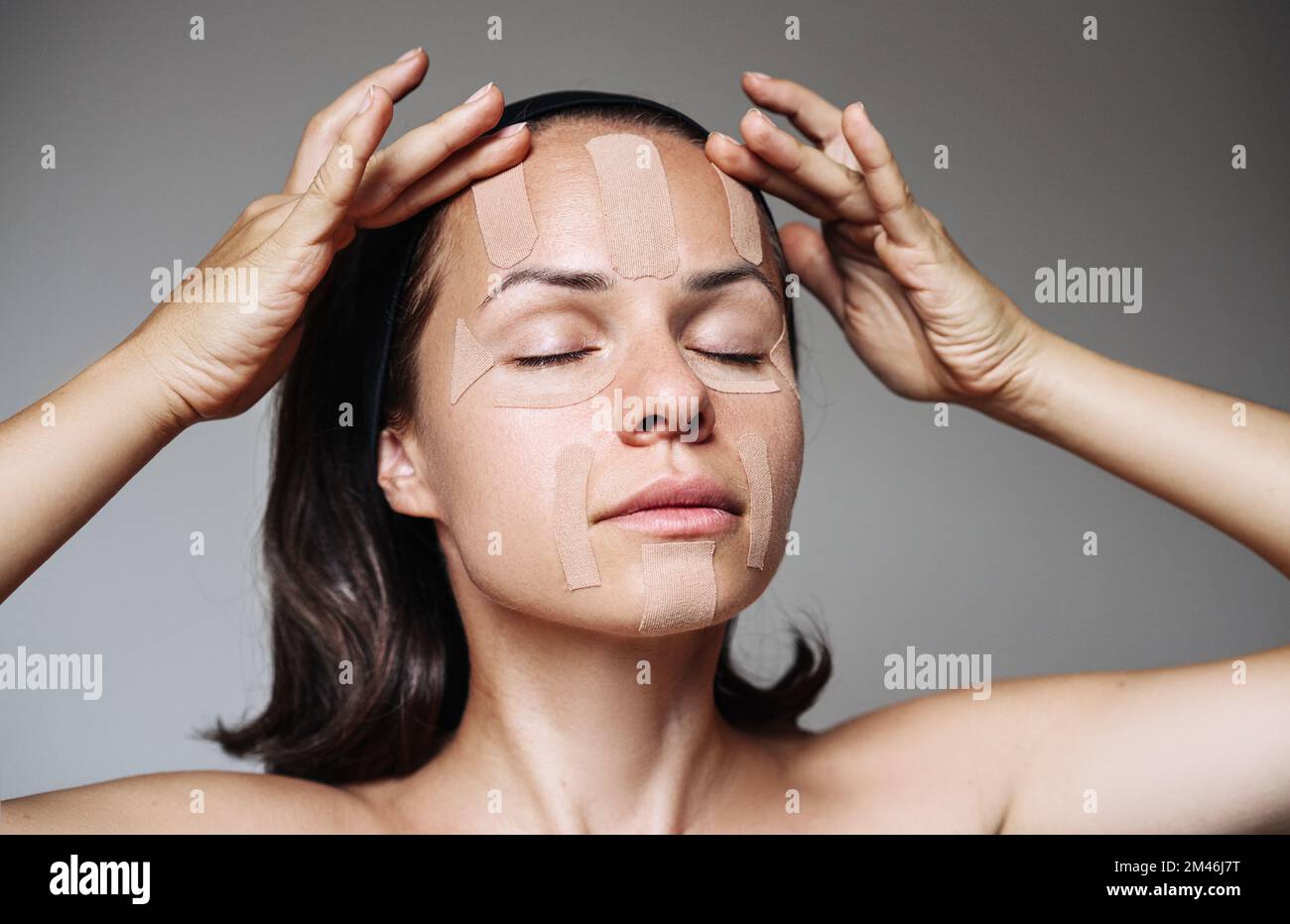 Young adult woman applying facial kinesiology tape on her face, facial ...