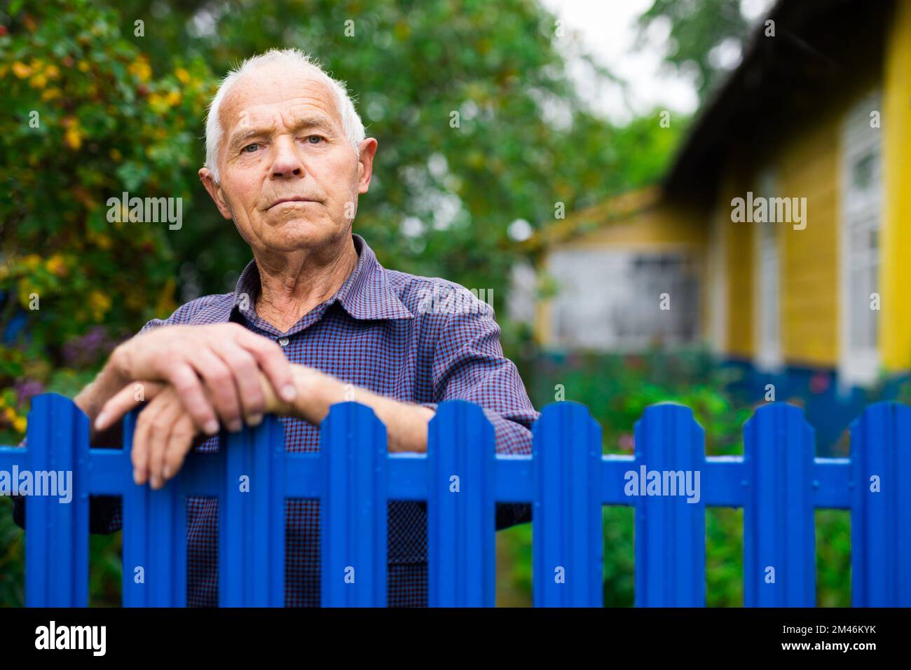 Portrait of pensive elderly man at fence of his country house in ...