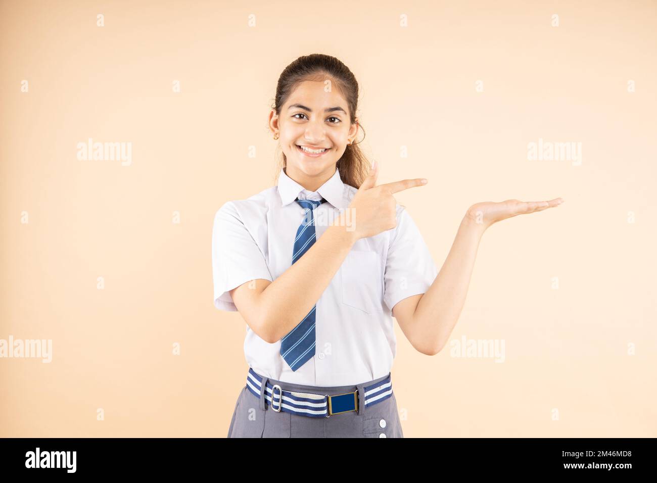 Happy Indian student schoolgirl wearing school uniform pointing at ...