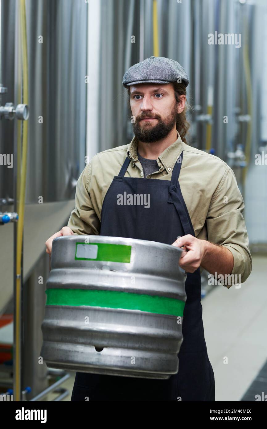 Portrait of microbrewery worker carrying keg with beer to warehouse ...