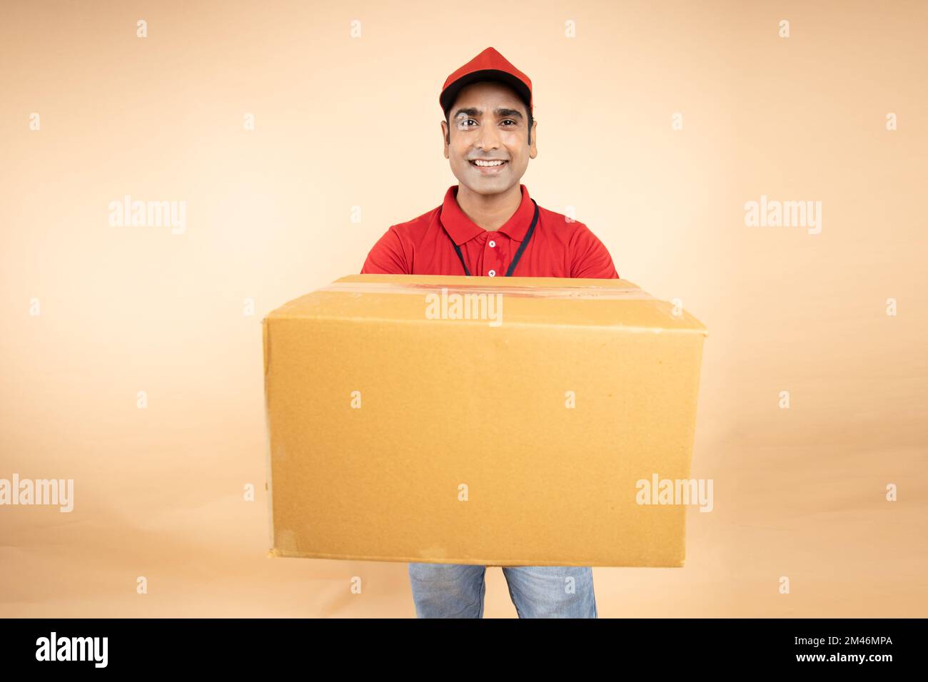 Portrait of happy Indian delivery man in red cap and T-shirt hold ...