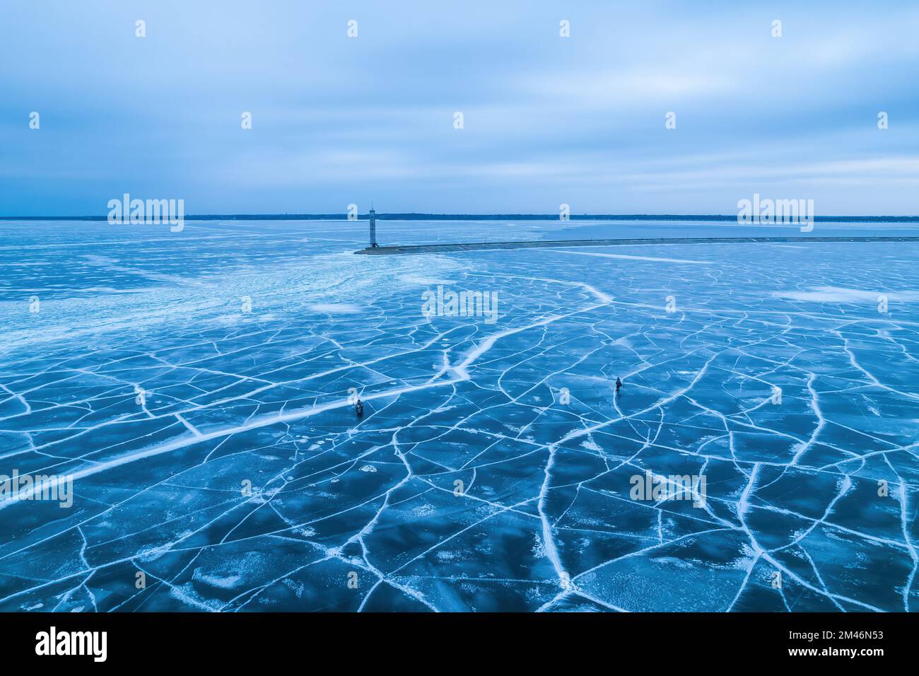 Frozen lake, blue ice with cracks. Fishermen are fishing, a lighthouse ...