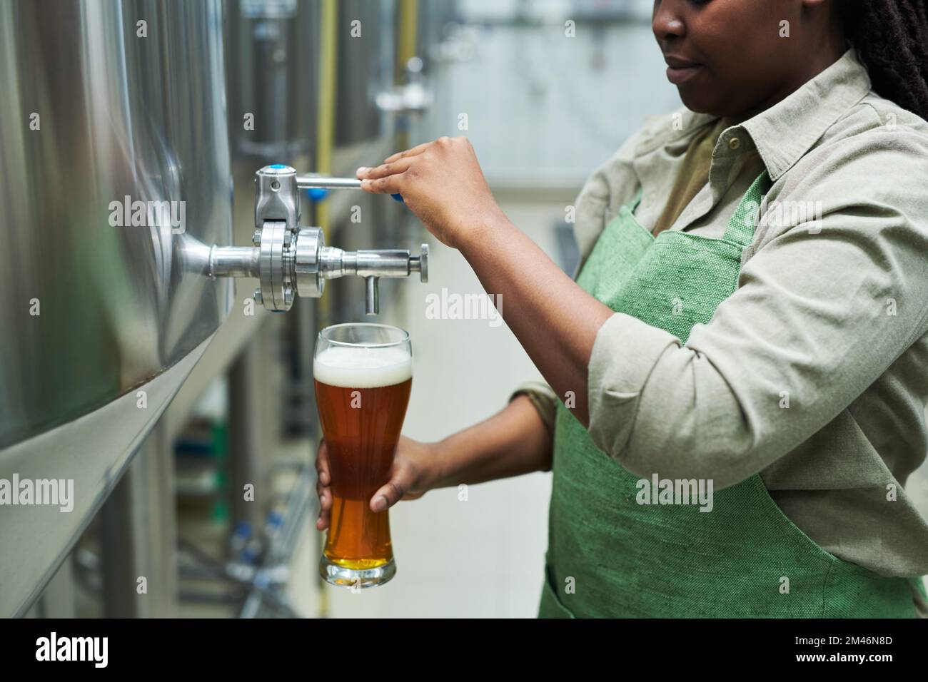 Cropped image of brewery worker filling big glass with beer from tank ...