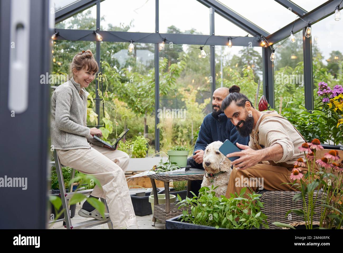 Smiling friends sitting in greenhouse Stock Photo - Alamy