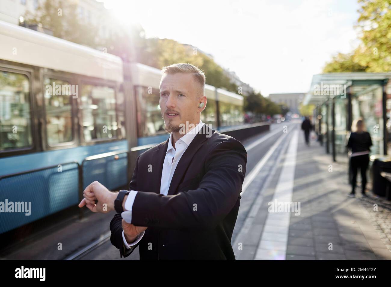 Businessman waiting at tram stop and checking watch Stock Photo - Alamy