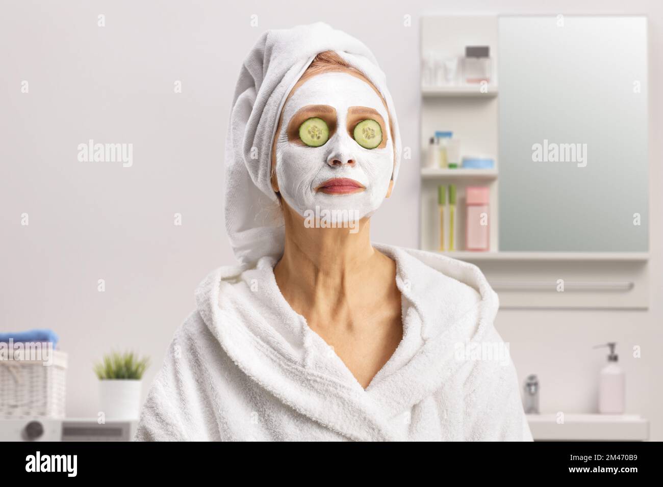 Woman in a bathrobe with a face mask with cucumber on eyes standing ...