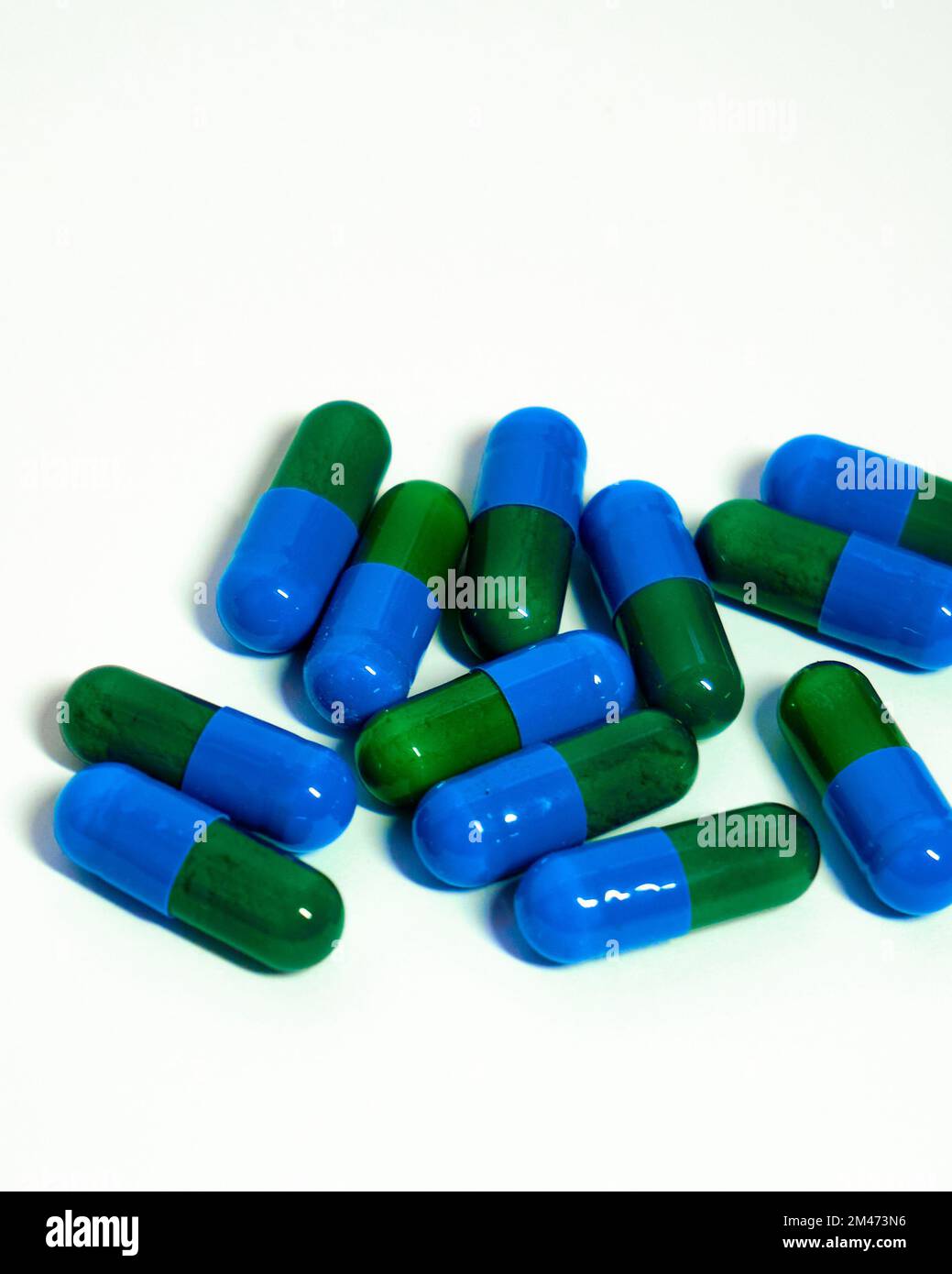 A vertical closeup shot of green and blue pills on the white background ...