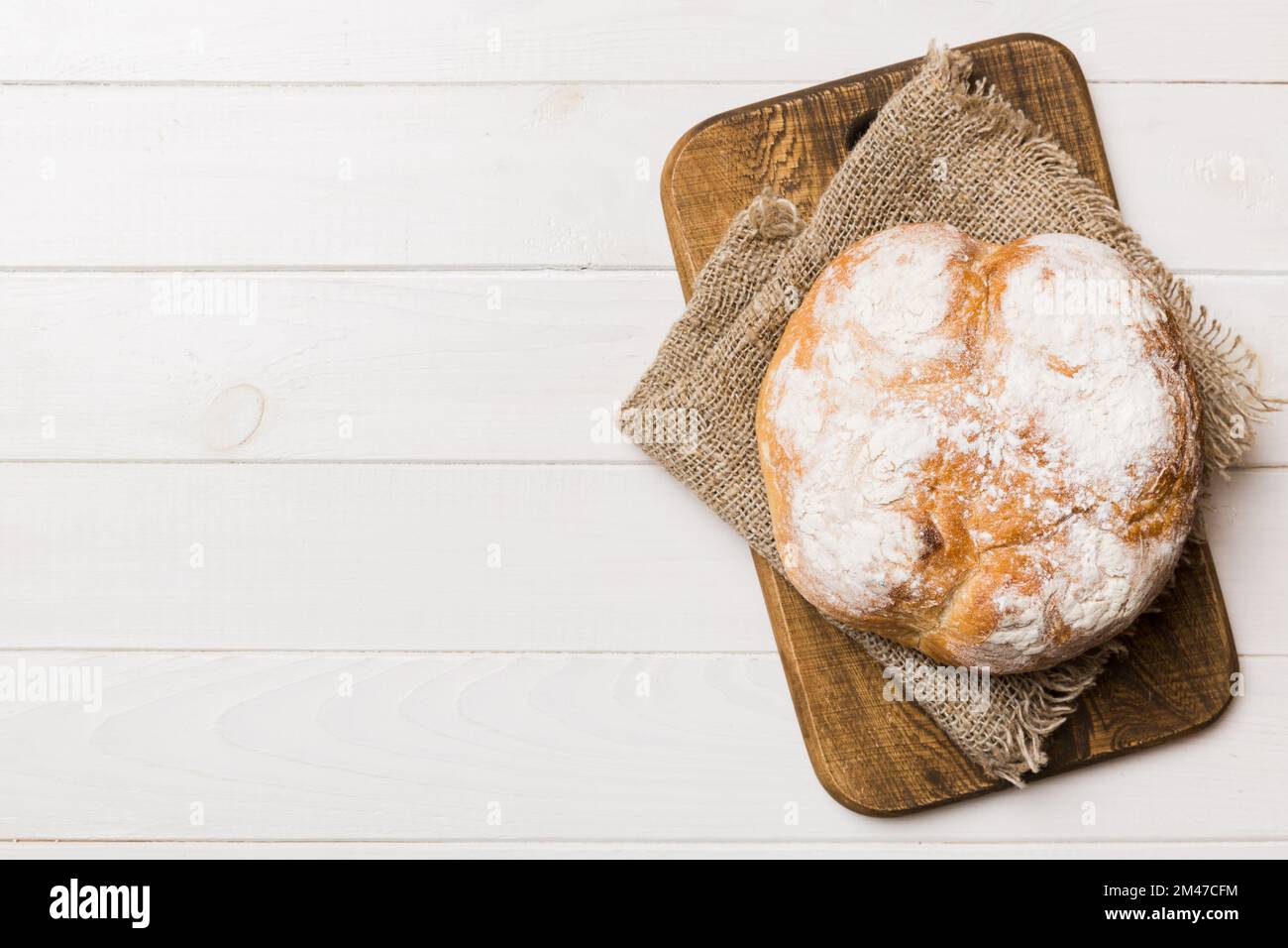 Freshly baked bread on cutting board against white wooden background ...