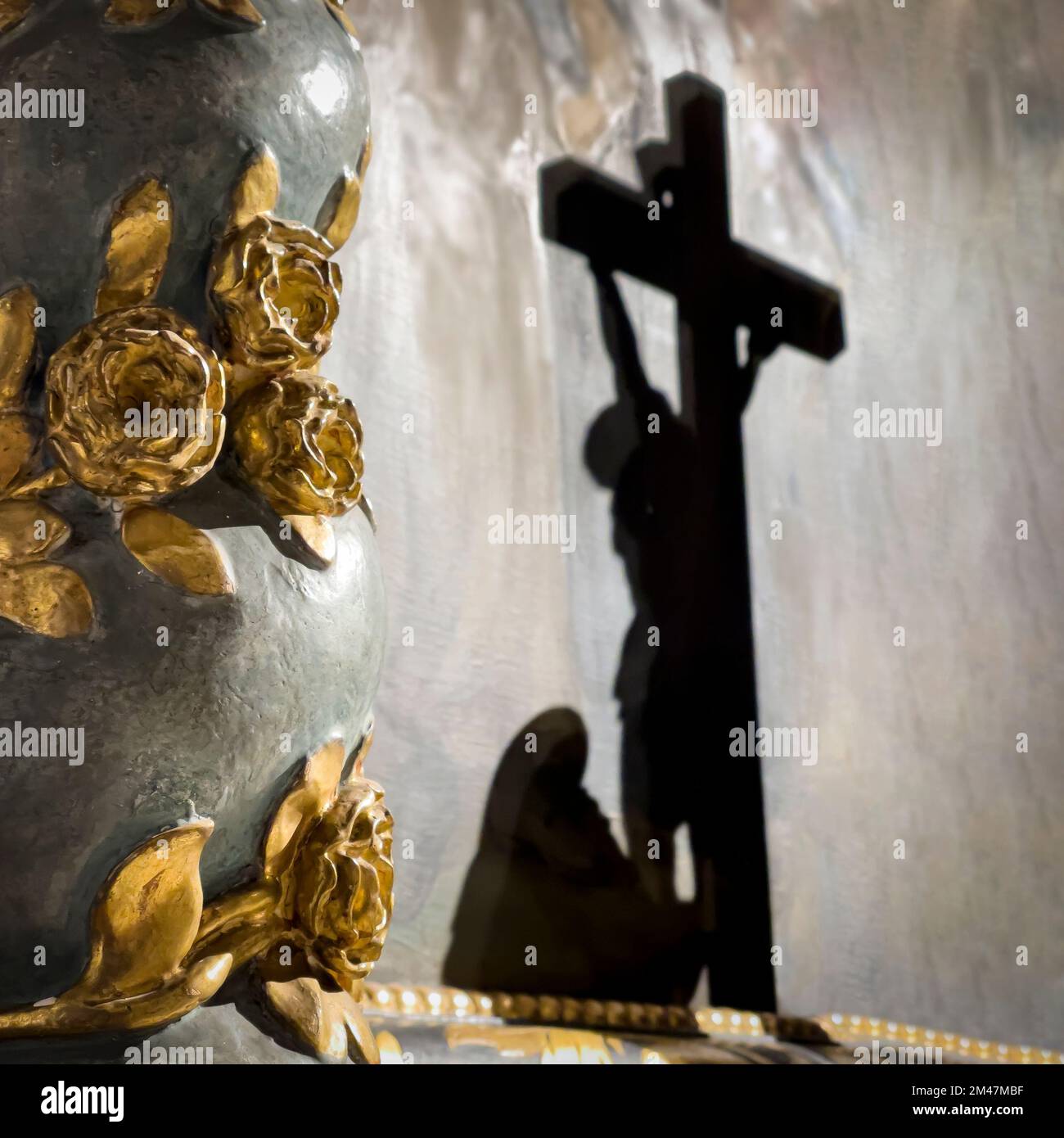A crucifix with a squatting person in front of it as a shadow cast. In ...