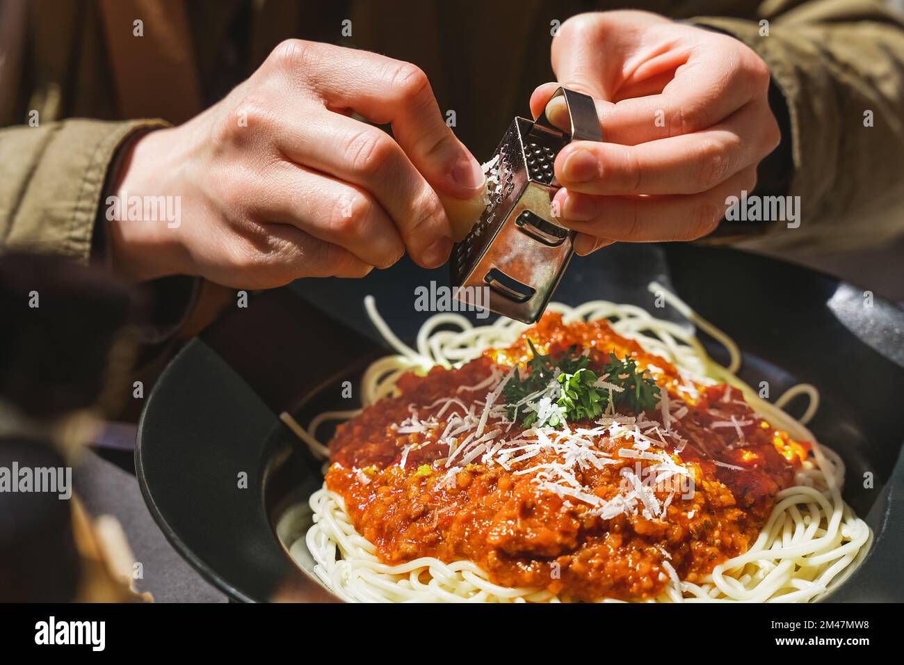 Hands grating delicious parmesan cheese on freshly made italian bolognese pasta. Small box of ...