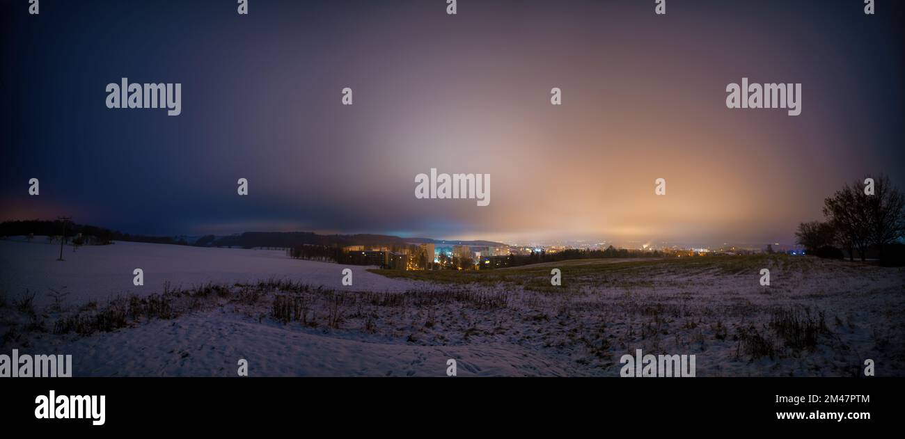 night landscape of a snowy field and a city with lights on the horizon ...