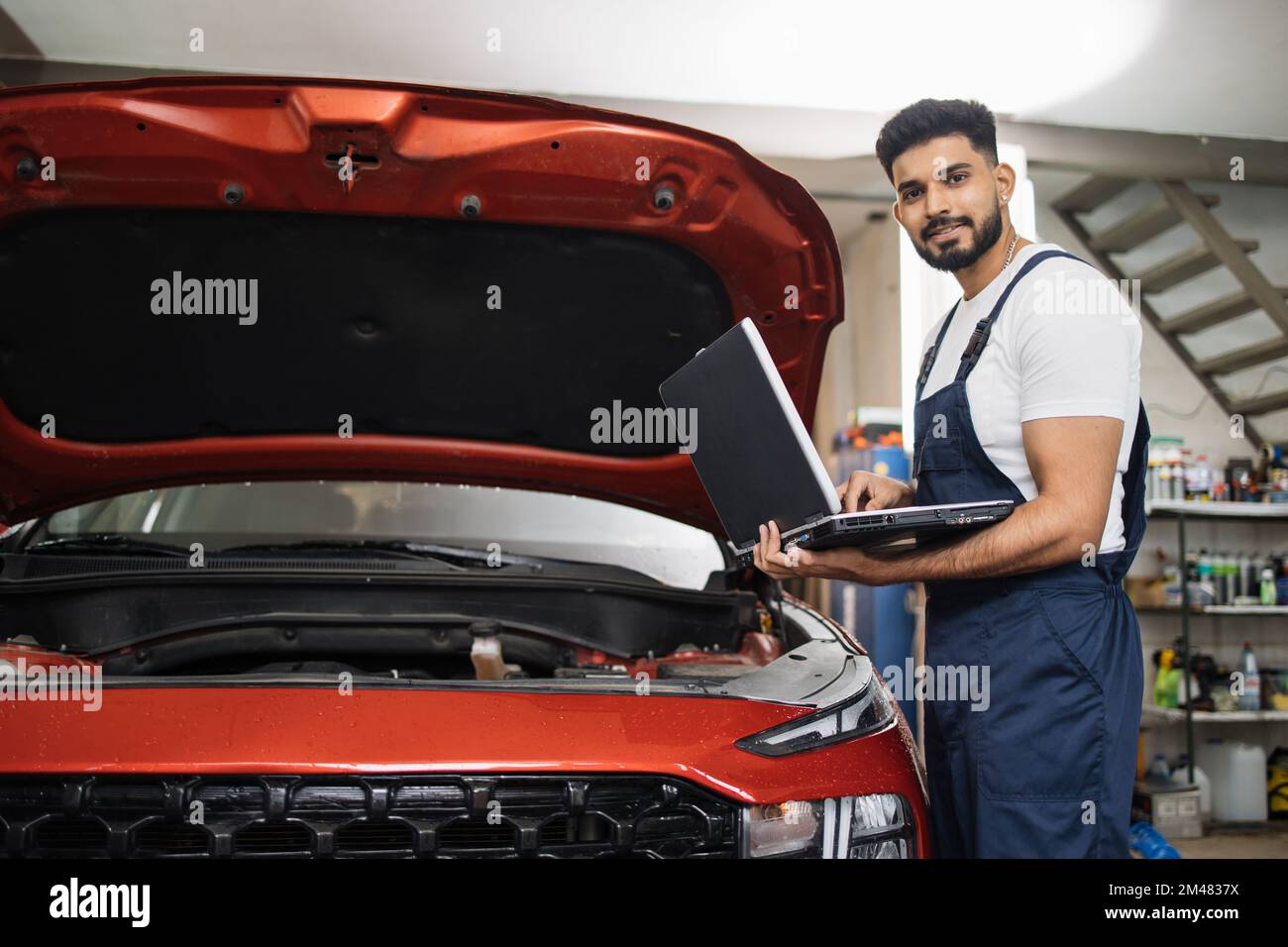 Young bearded man mechanic using laptop for auto diagnostics of sport ...