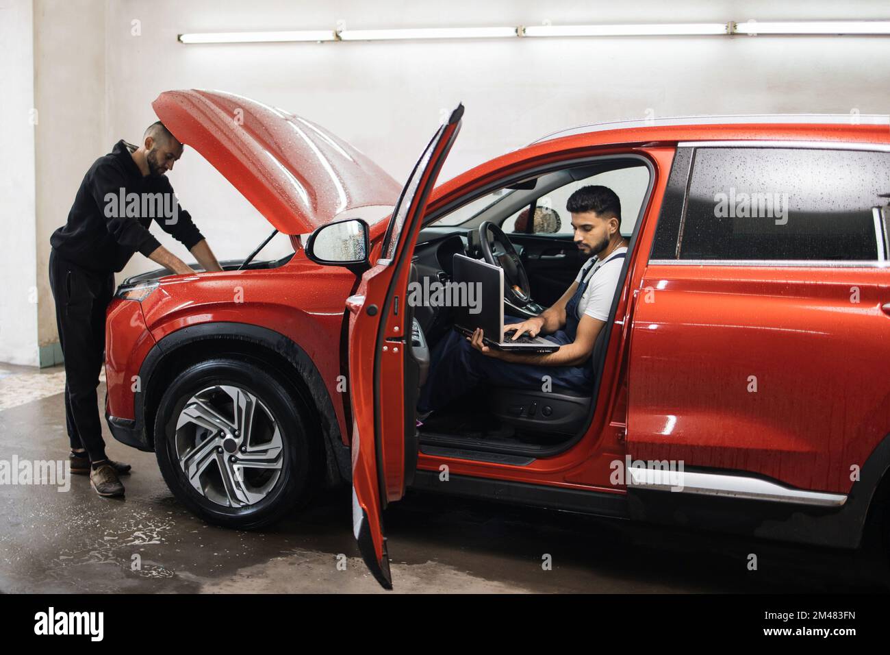 Young male mechanic using laptop sitting inside red car and his ...