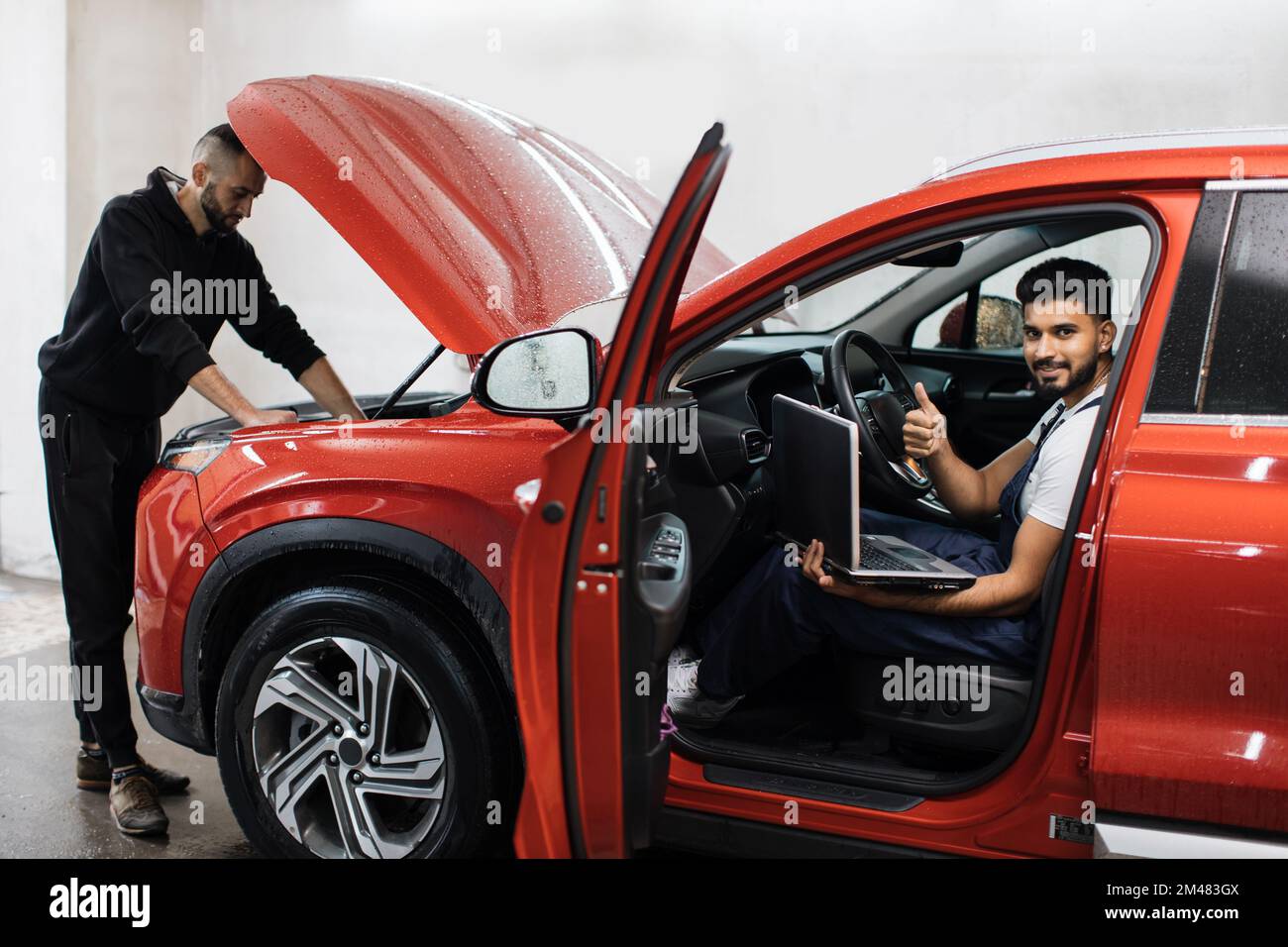Young male mechanic using laptop sitting inside red car and his ...