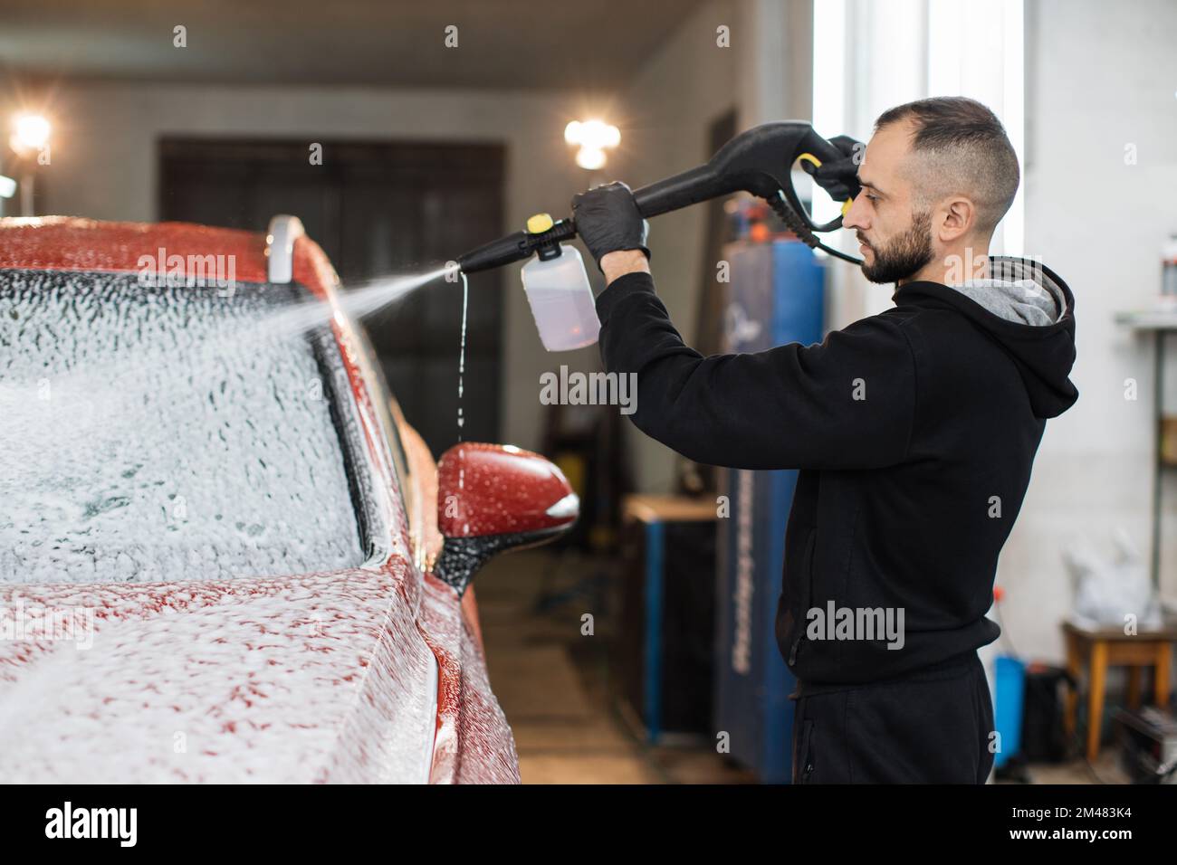 Bearded young man car wash worker spraying cleaning foam to a modern ...