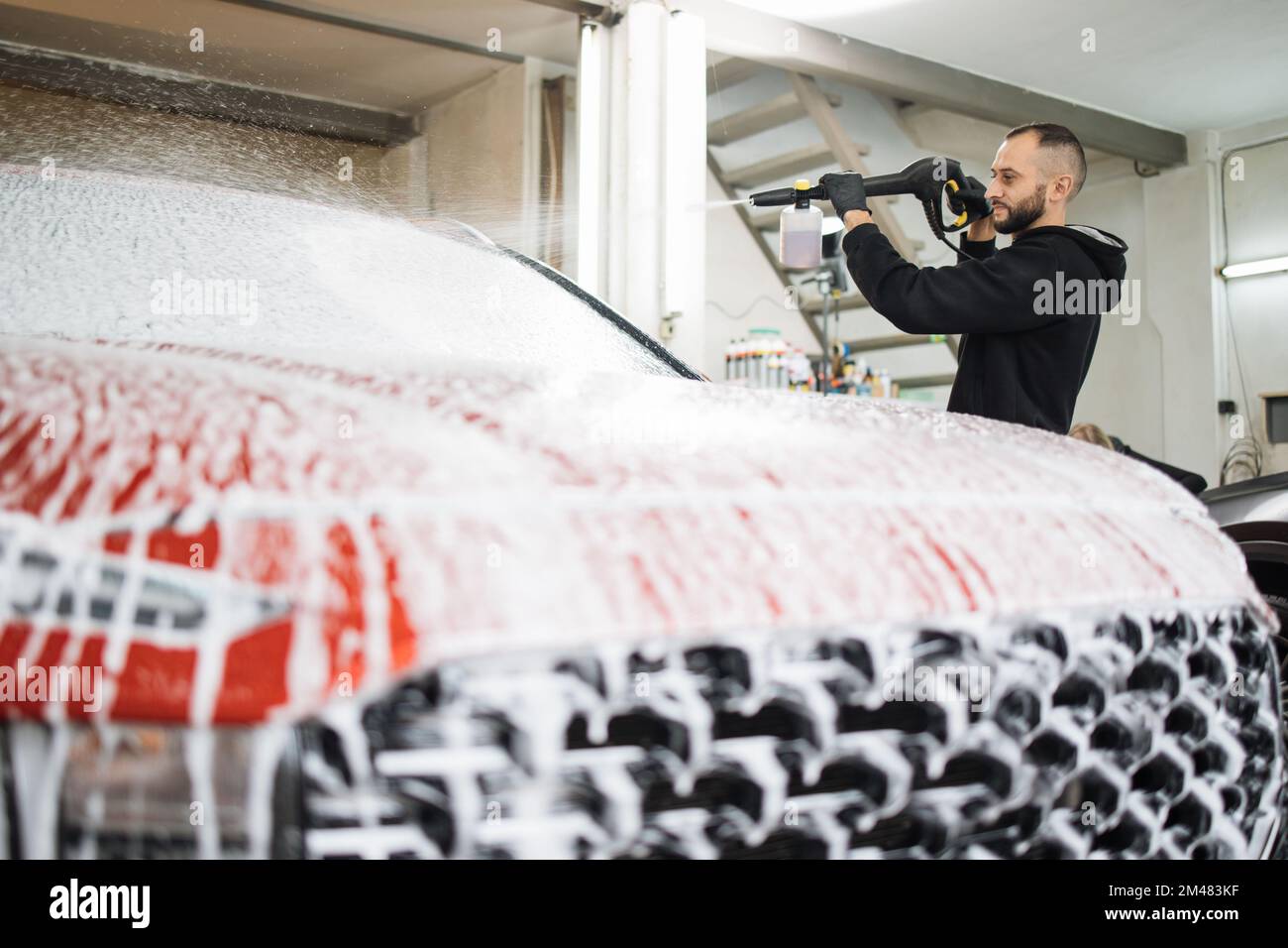 Bearded young man car wash worker spraying cleaning foam to a modern ...