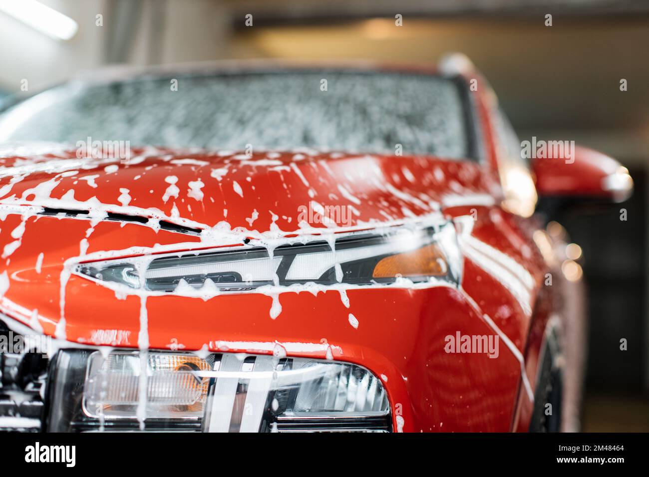 Washing a car headlight at auto wash service. Soapy red car. Washing of ...