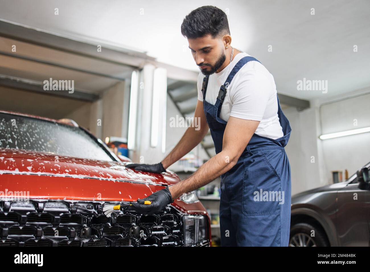 Handsome bearded male car wash worker cleaning red crossover grille ...