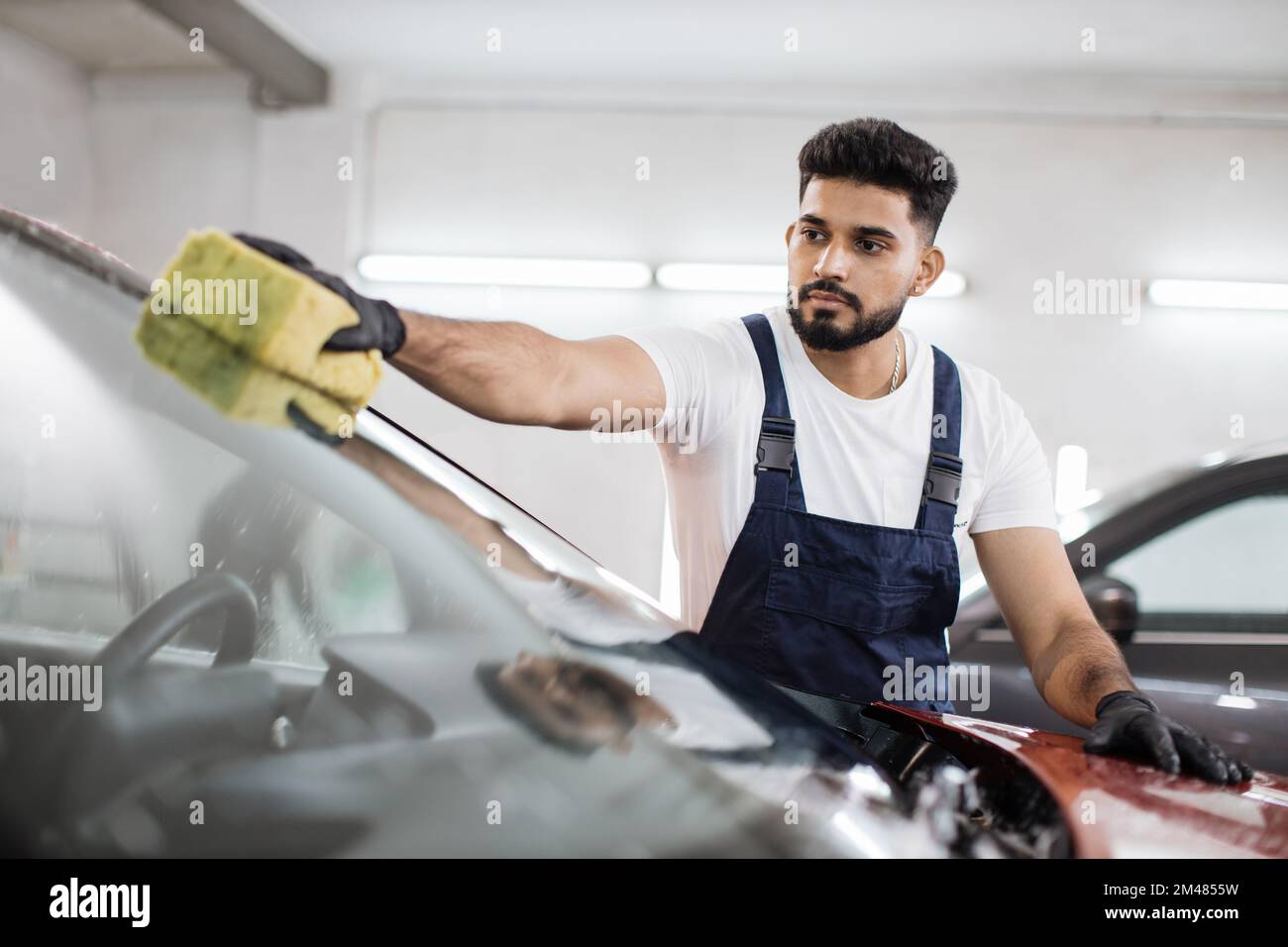 Young bearded man, car wash worker, wearing t-shirt and overalls ...