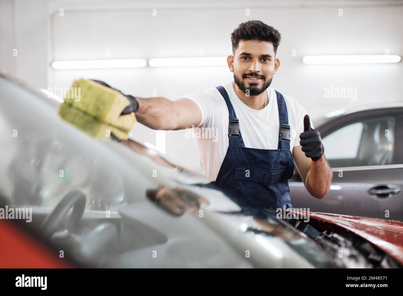 Young bearded man, car wash worker, wearing t-shirt and overalls ...
