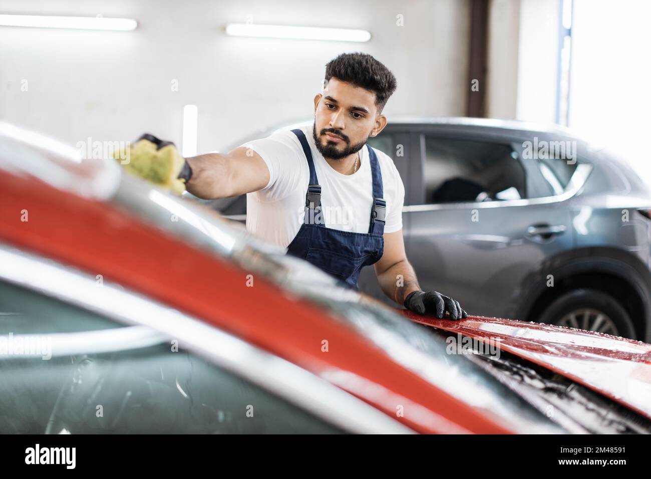 Young bearded man, car wash worker, wearing t-shirt and overalls ...