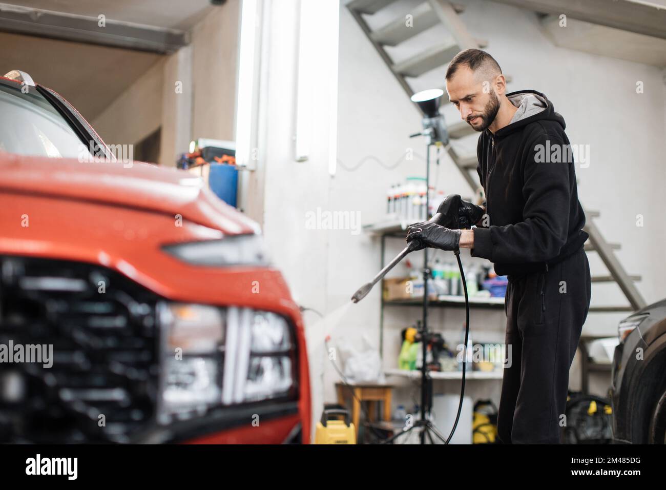Young good-looking bearded man worker washing luxury red crossover car ...