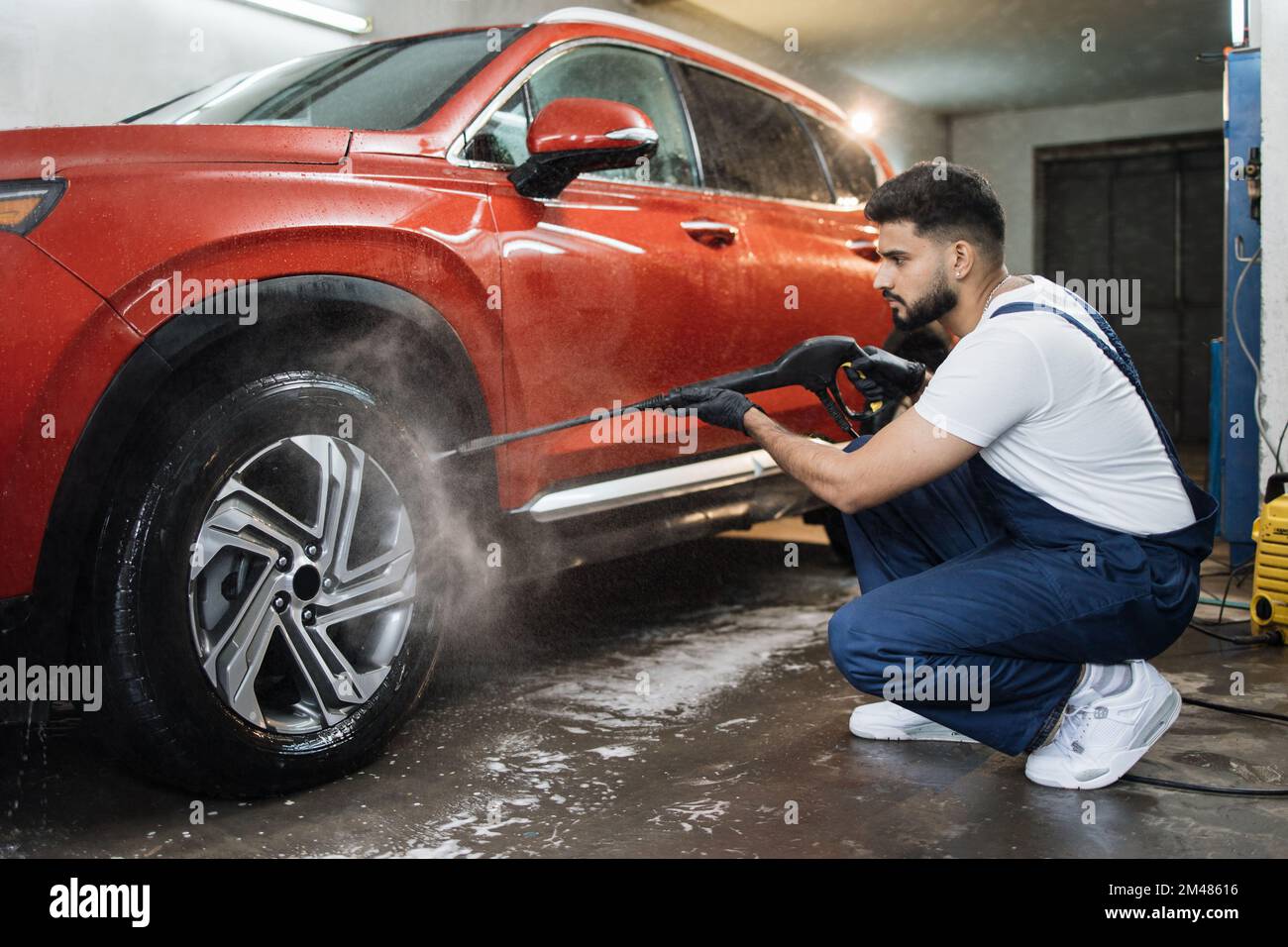 Side view portrait of young bearded male worker washing the car wheels ...
